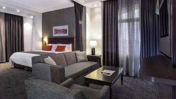 Quarto de hotel com uma cama, um sofá, uma mesa de centro e uma televisão.