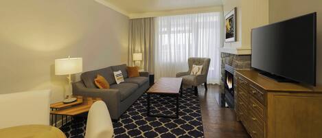 Quarto de hotel com sofá, poltrona, televisão e lareira.