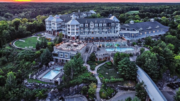 Um hotel grande, com vários andares, piscina, jardins ajardinados e uma vista panorâmica para o pôr do sol.