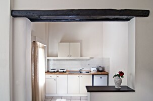 Uma cozinha compacta com armários brancos, bancada de madeira, pia, torradeira e um vaso com uma flor.