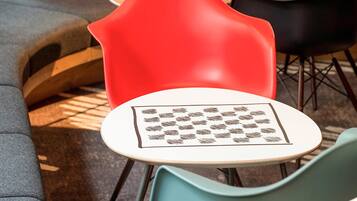 Uma área de estar moderna com uma cadeira vermelha, uma mesa redonda com toalha de mesa estampada e um sofá cinzento.