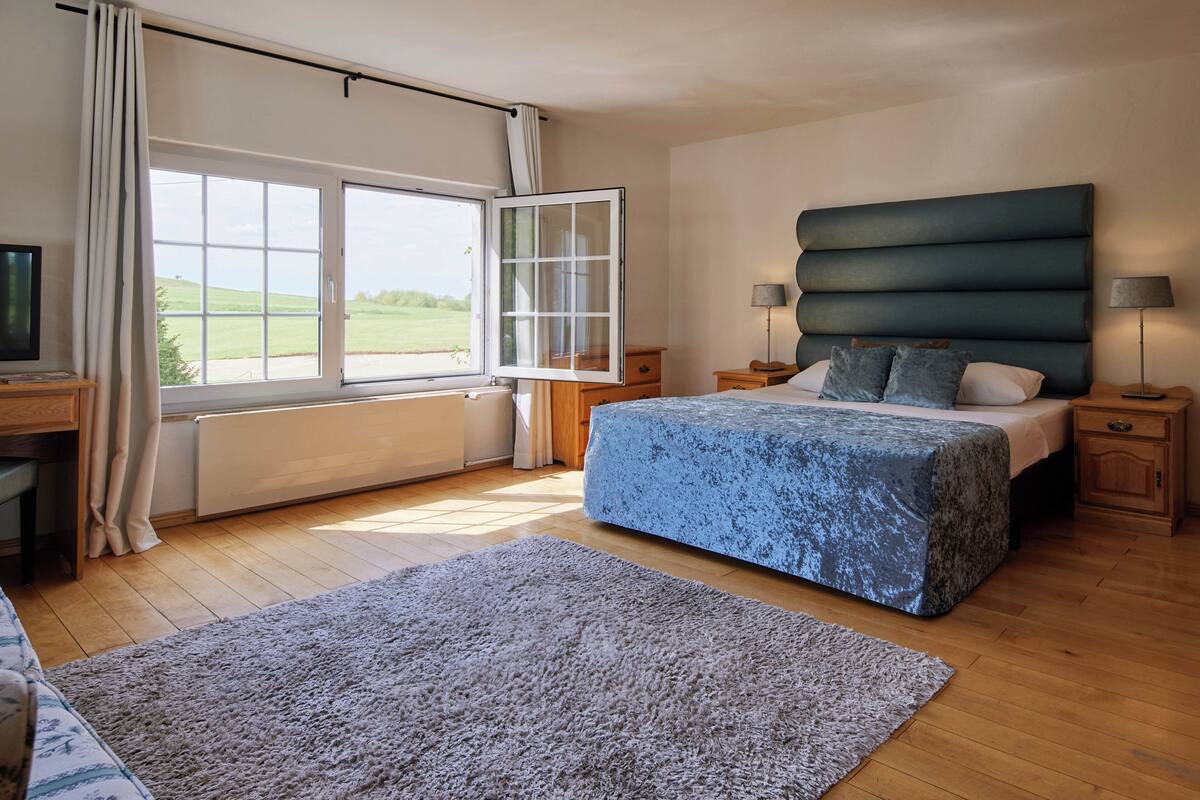 Quarto com uma cama grande, escrivaninha, cadeira, janela com cortinas e vista para o exterior.