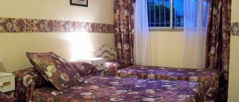 Quarto com duas camas, mesa de cabeceira, abajur e janela com cortinas.