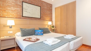 Quarto de hotel com parede de tijolos, uma cama grande com um laptop, duas luminárias de cabeceira e um guarda-roupa de madeira.