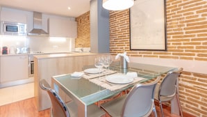 Uma cozinha moderna com mesa de jantar de vidro, eletrodomésticos de aço inoxidável e parede de tijolos.