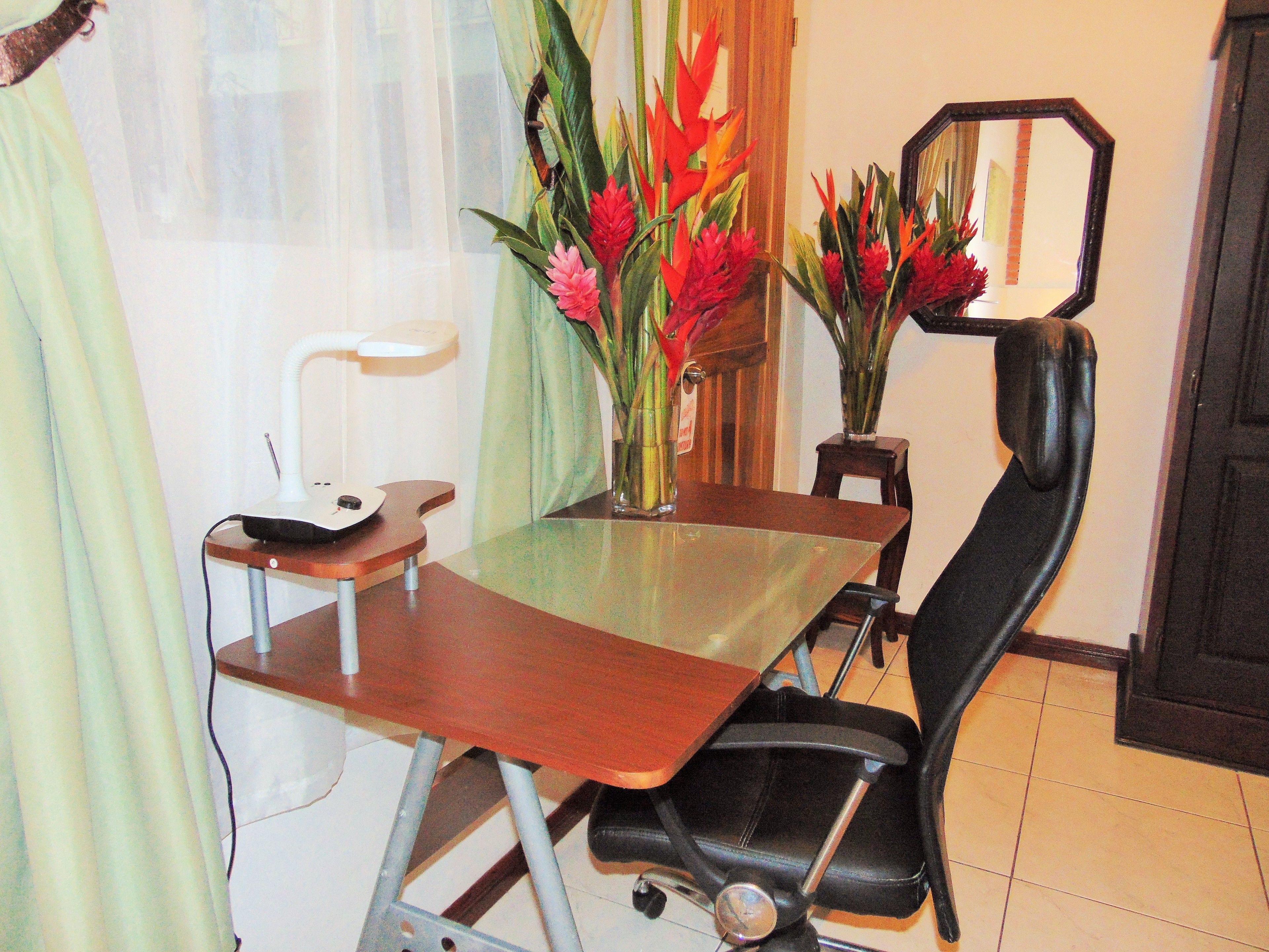 Uma sala de jantar com uma mesa, cadeiras, uma poltrona com apoio para os pés, um espelho e um vaso com flores.