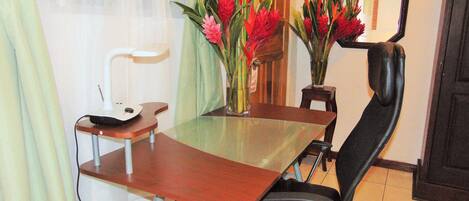 Uma sala de jantar com uma mesa, cadeiras, uma poltrona com apoio para os pés, um espelho e um vaso com flores.