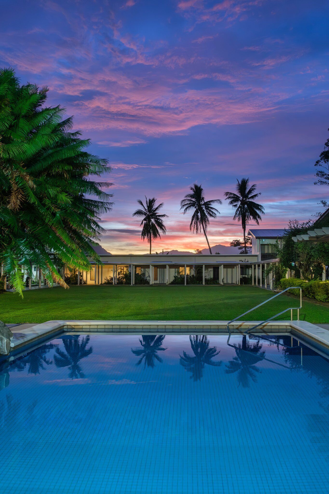 Piscina com vista desobstruída da paisagem circundante, incluindo palmeiras e um edifício com telhado plano.