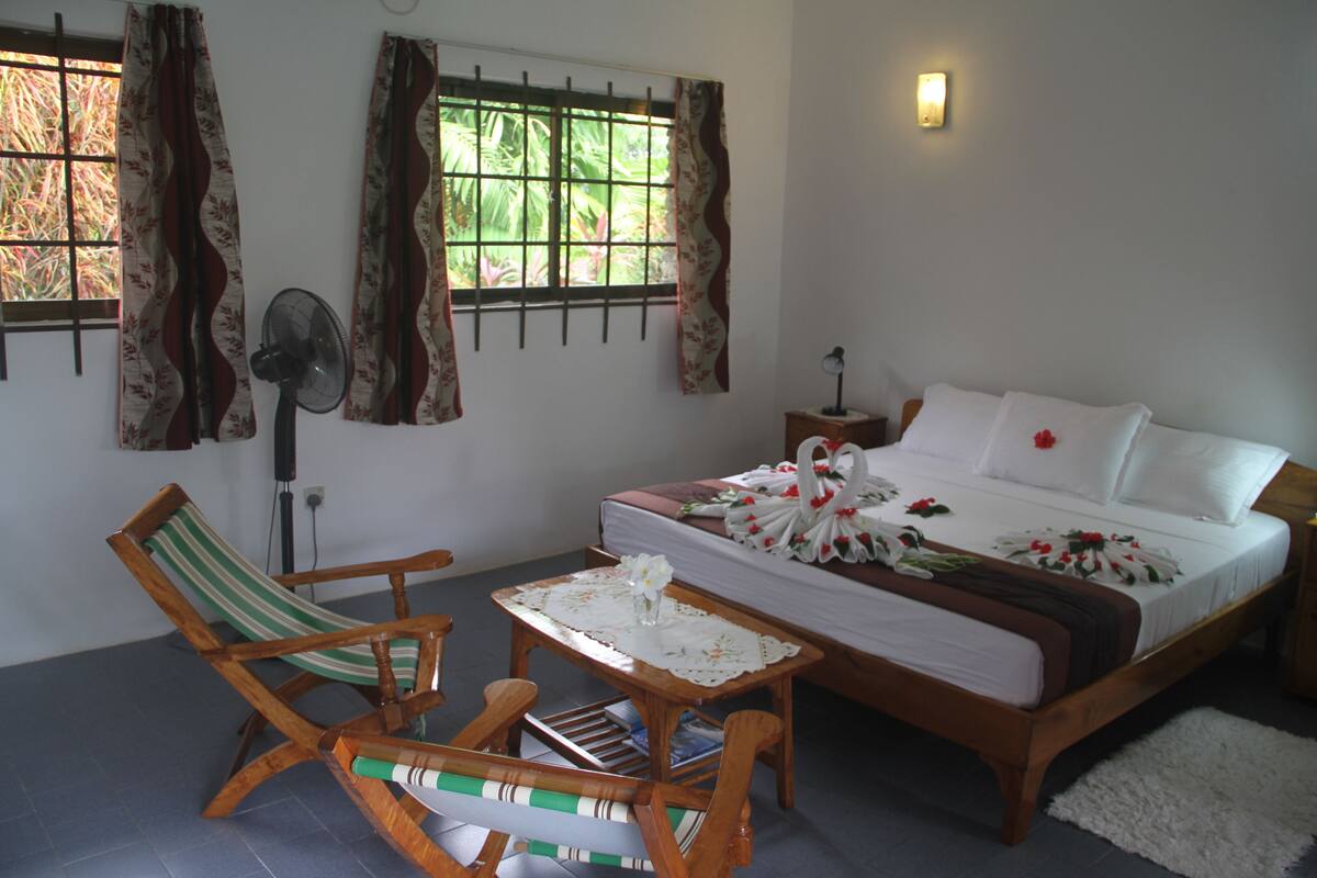 Quarto com cama, cadeira, mesa e ventoinha.