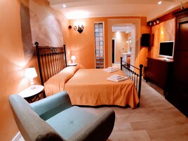 Quarto de hotel com cama, uma cadeira, televisão e banheiro visível por uma porta aberta.