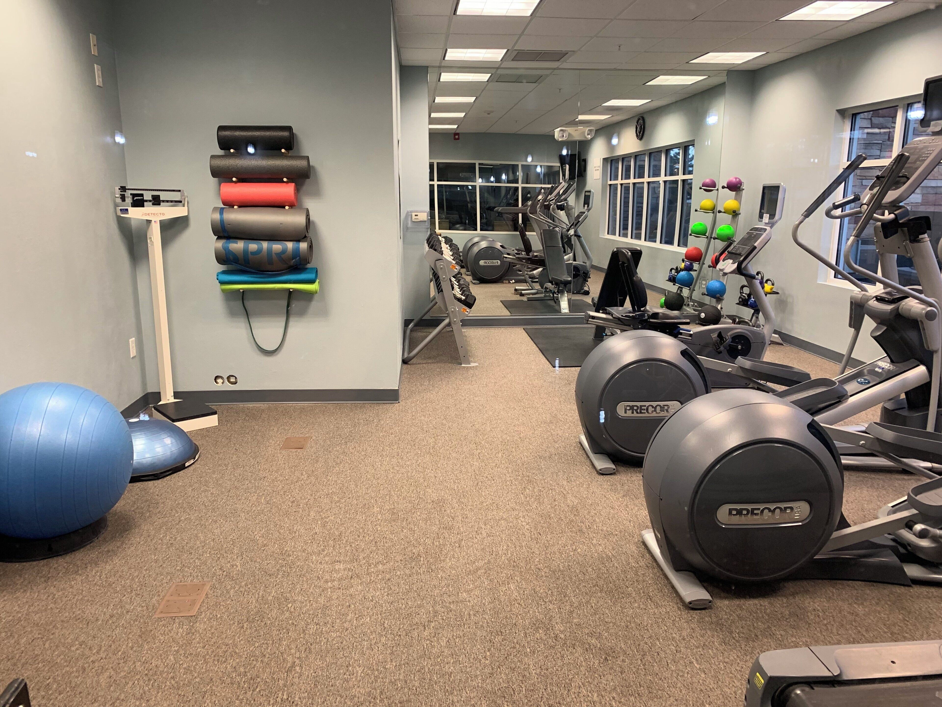 Academia com equipamentos de ginástica, um aparelho de musculação fixado na parede e uma bola de exercício azul grande.