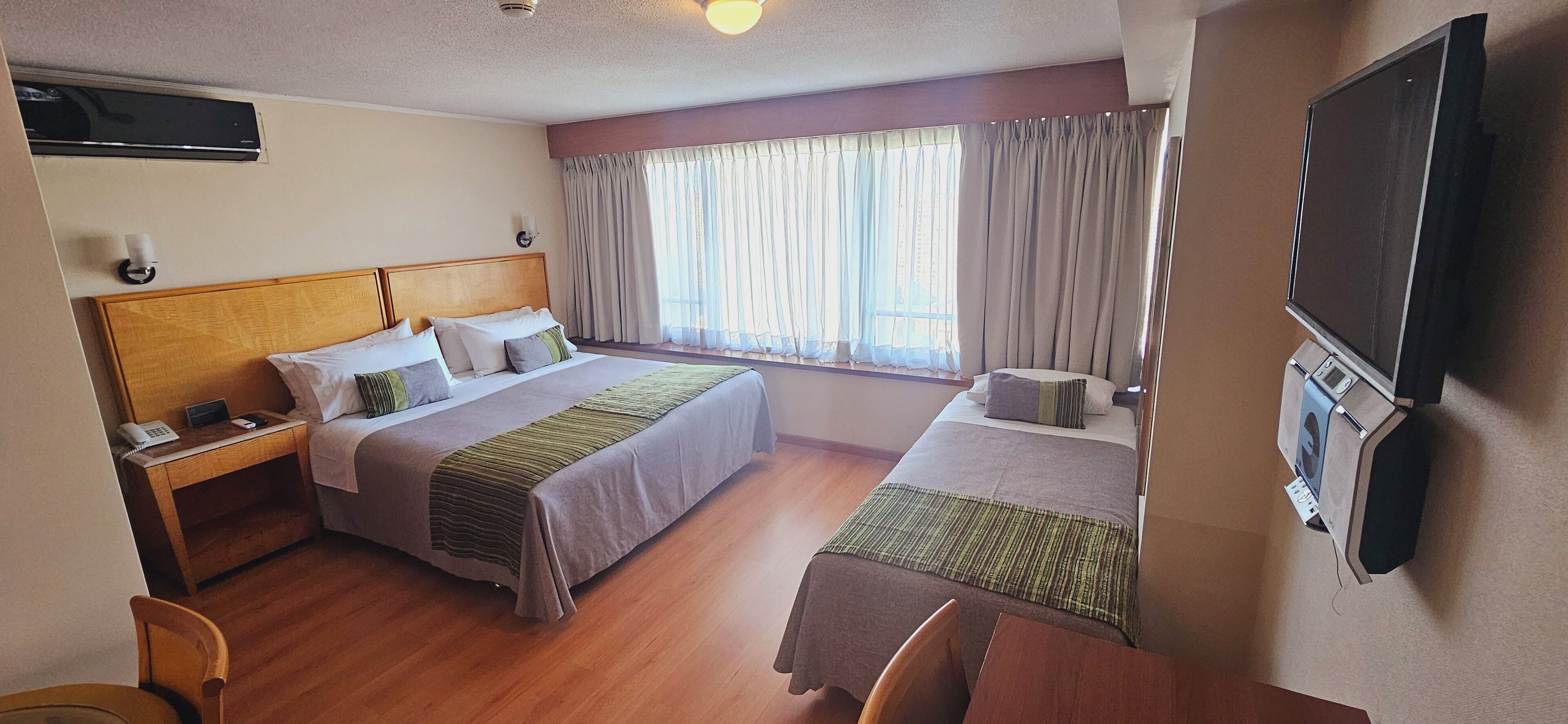 Quarto de hotel com duas camas, televisão, escrivaninha com telefone e janela com cortinas.