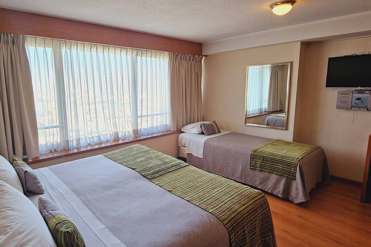 Quarto de hotel com duas camas, televisão, espelho e janela com cortinas.