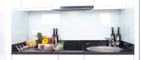 Cozinha moderna com armários brancos, bancada preta e coifa de aço inoxidável. Há vários utensílios e garrafas na bancada.