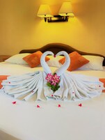Cama bem arrumada com um centro de toalhas em formato de cisne e almofadas laranja.