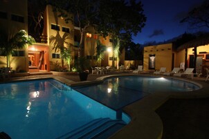 Piscina com espreguiçadeiras e um edifício com varanda.