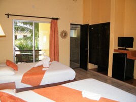 Quarto de hotel com duas camas, televisão, minibar e porta de vidro deslizante para área externa com mesa e cadeiras.