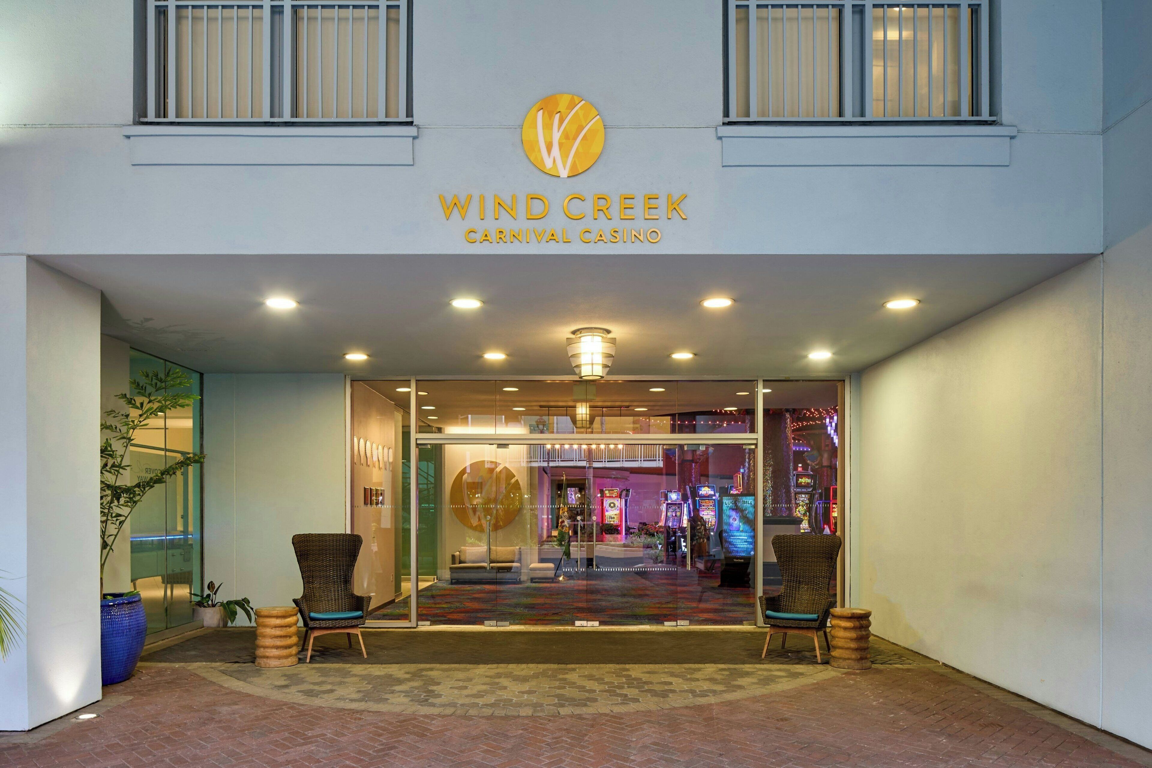 Entrada do Wind Creek Carnival Casino, com fachada de vidro, área de estar interna e um letreiro sobre a entrada.
