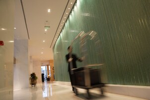 Um corredor com parede verde com textura, piso polido e uma pessoa empurrando um carrinho.