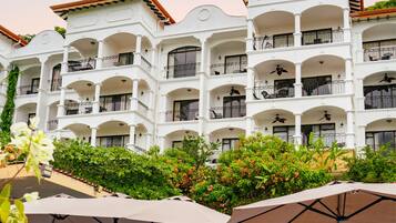 Um hotel com piscina, área de estar ao ar livre e um edifício grande com várias varandas.
