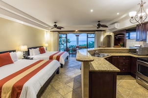 Quarto de hotel com duas camas, uma cozinha compacta e varanda com vista para o mar.