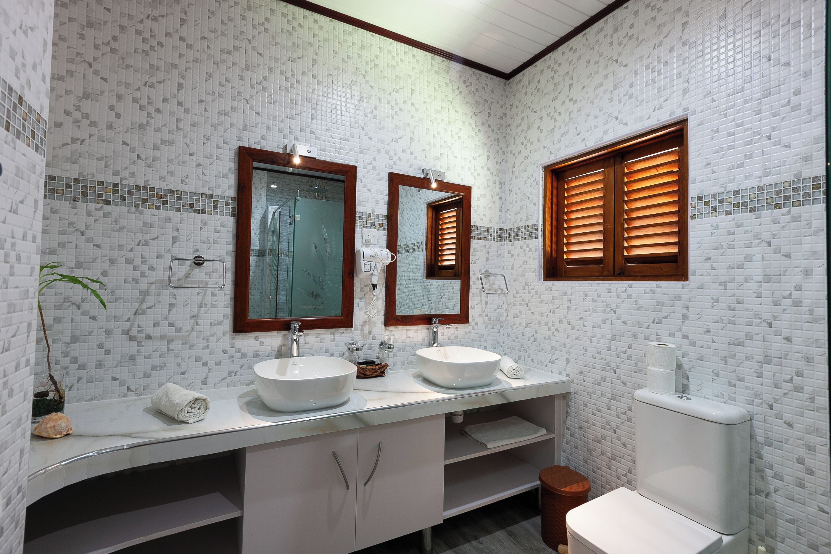 Casa de banho com duas pias, sanita e janela com estores.