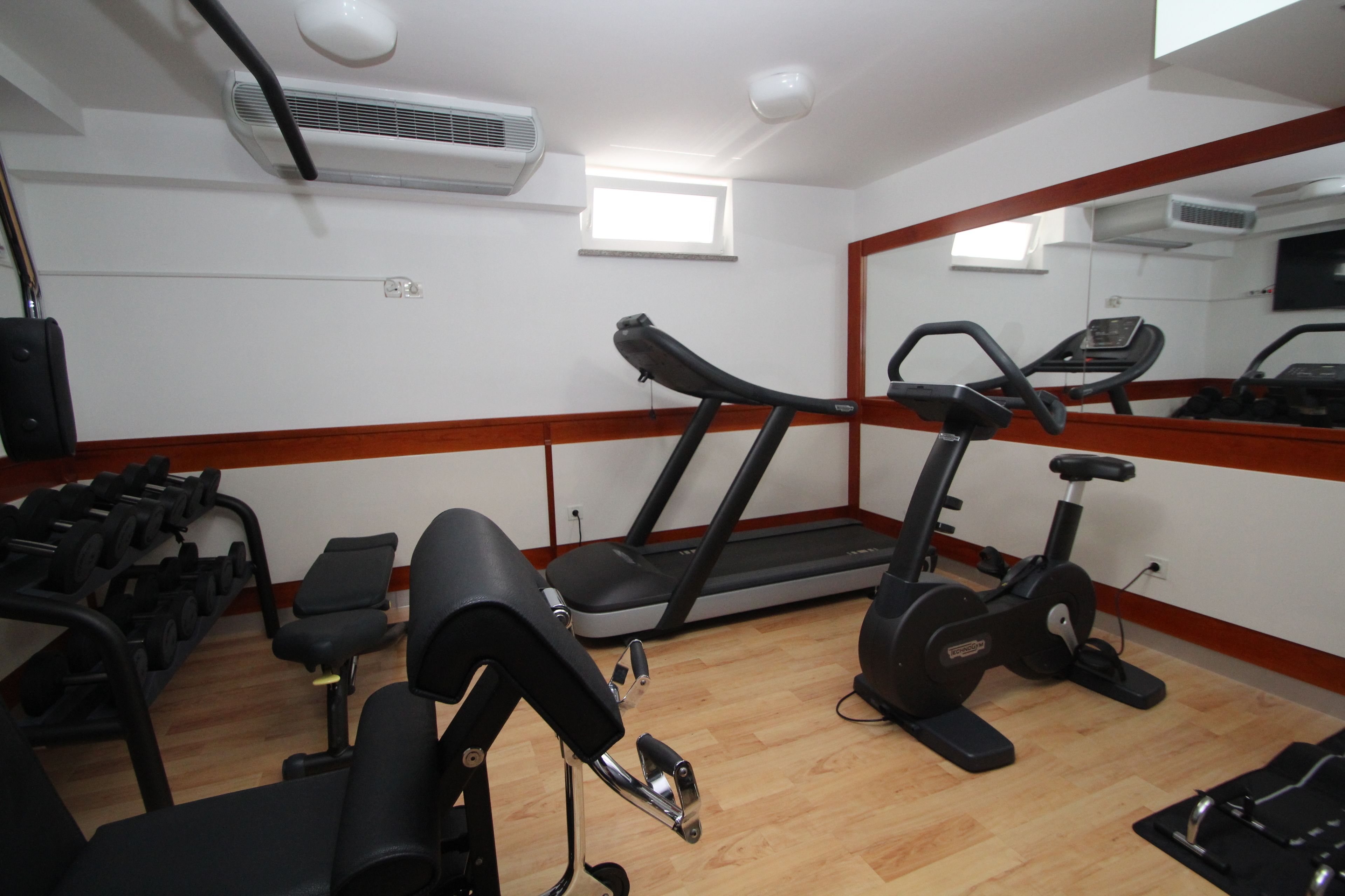 Uma academia com equipamentos de ginástica, esteira e espelho na parede.