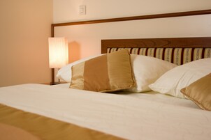 Cama bem arrumada com cabeceira de madeira e luminária ao lado.