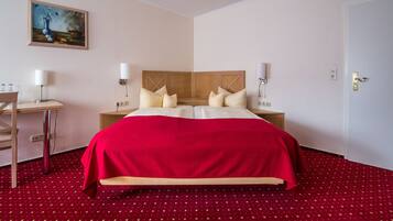 Quarto de hotel com uma cama grande, duas mesas de cabeceira, uma escrivaninha e um quadro na parede.