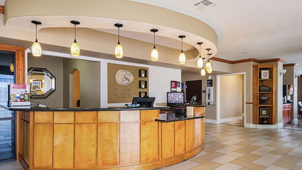 Uma área de recepção de hotel com um balcão curvo de madeira, um relógio e uma placa indicando 'Comfort Suites'.