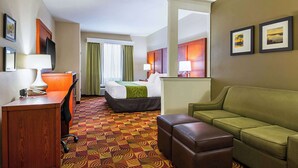 Quarto de hotel com cama, sofá verde, escrivaninha com abajur e carpete estampado.