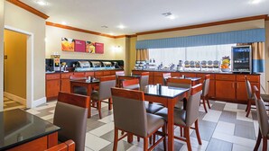 Uma sala de jantar de hotel com várias mesas e cadeiras, um buffet e uma televisão exibindo o menu.