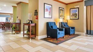 Um saguão de hotel com uma mesa de recepção, poltronas azuis, um tapete estampado e quadros nas paredes.
