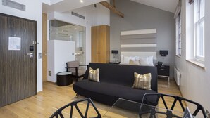 Uma sala de estar moderna com um sofá preto, piso de madeira e uma janela grande.