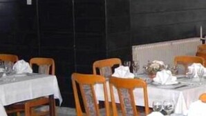 Interior de restaurante com mesas postas para refeições, cadeiras e parede revestida de azulejos pretos.