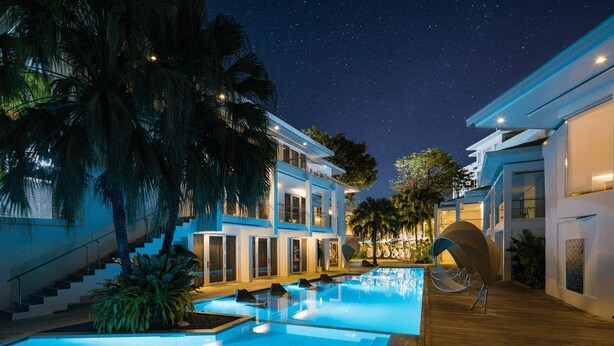 Um hotel moderno com piscina, palmeiras e céu noturno.