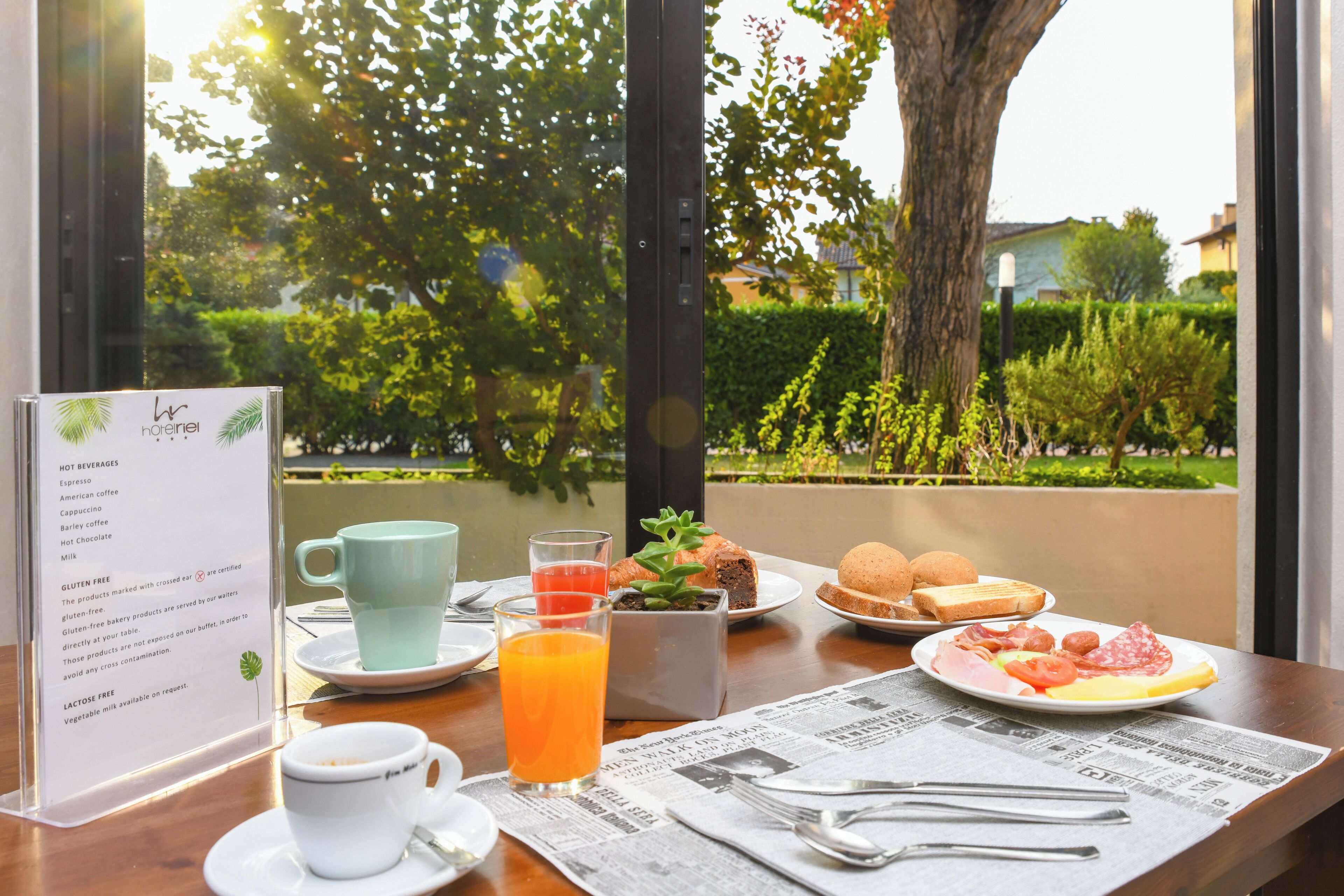 Mesa de café da manhã com um menu, uma xícara de café, um copo de suco de laranja, um prato de comida e um jornal.