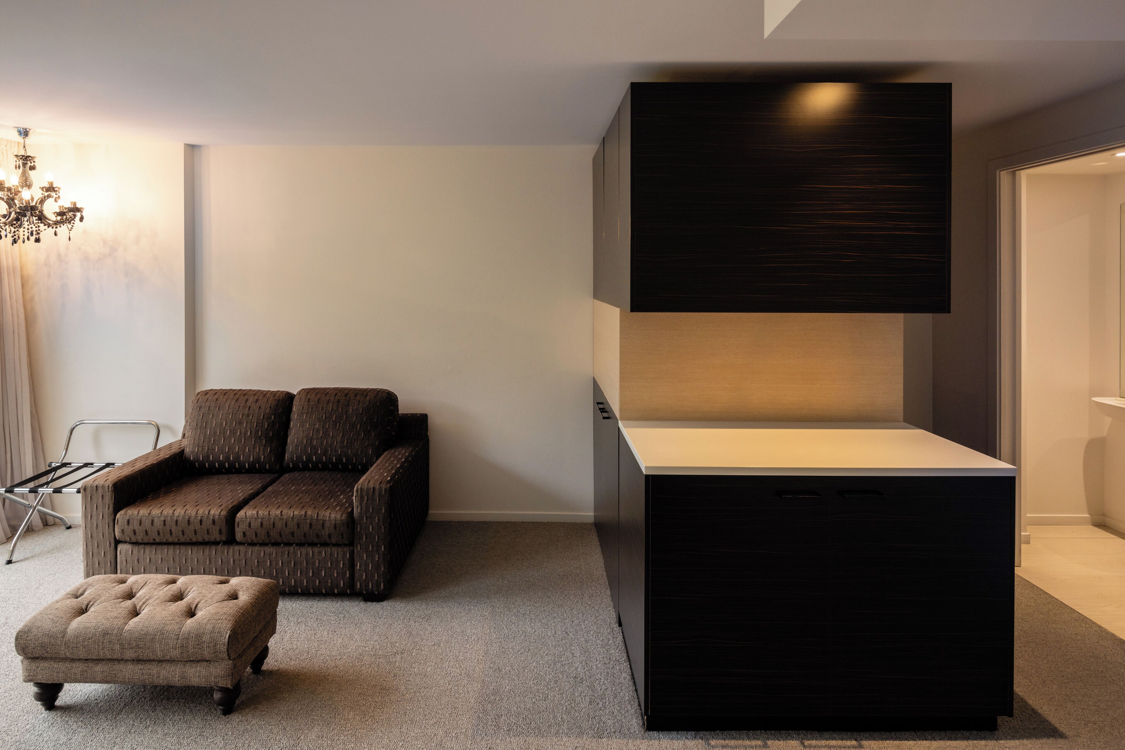 Uma sala de estar moderna com sofá, banquinho e um armário embutido preto.