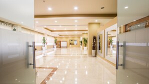 Um hall de hotel com piso de mármore polido, portas de vidro e plantas em vasos.