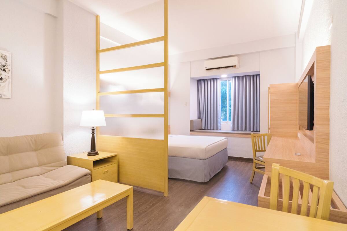 Quarto de hotel com sofá, escrivaninha, cadeira, cama e televisão.