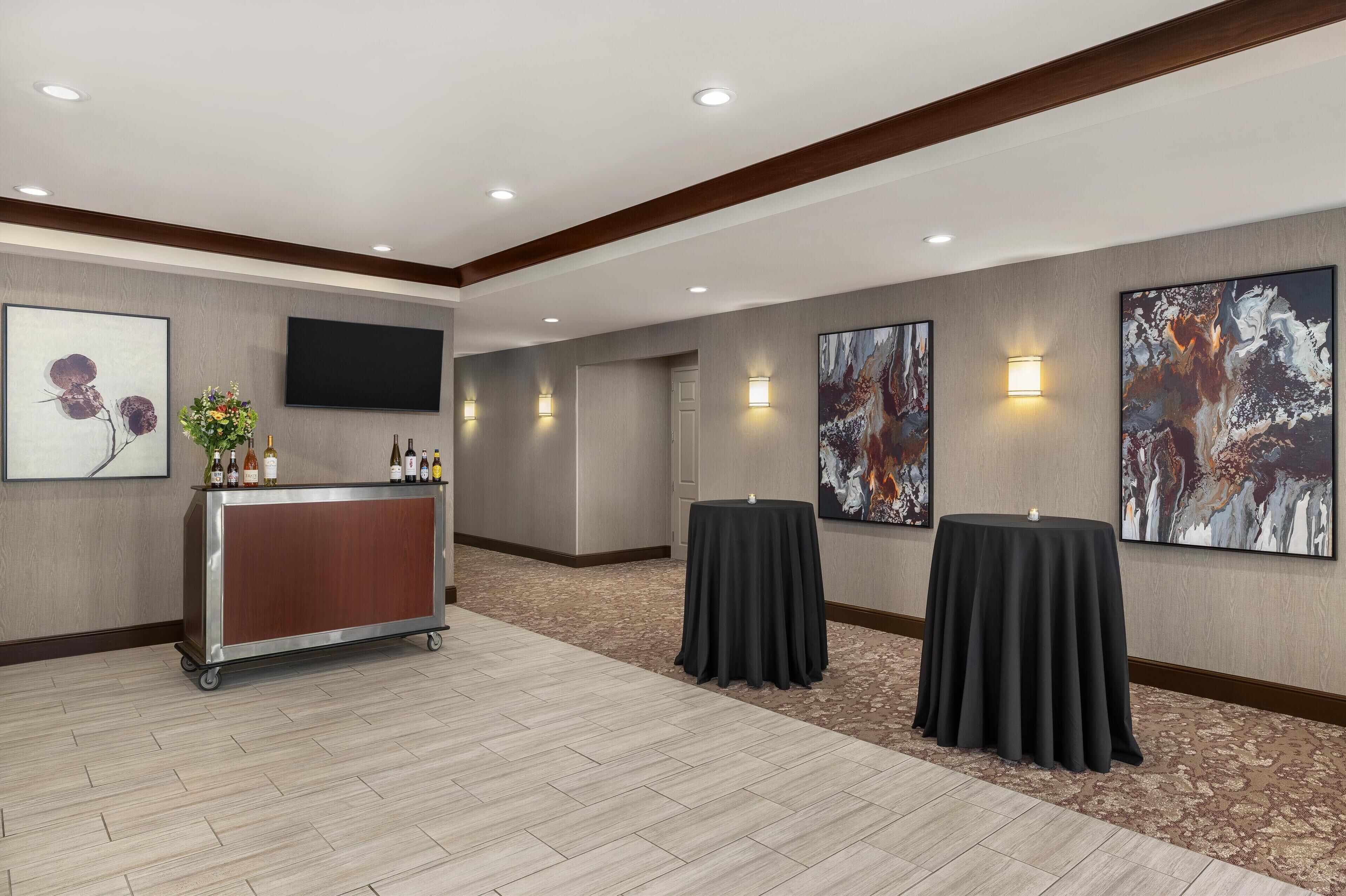 Um saguão de hotel com uma mesa de recepção, duas mesas redondas e pinturas abstratas nas paredes.