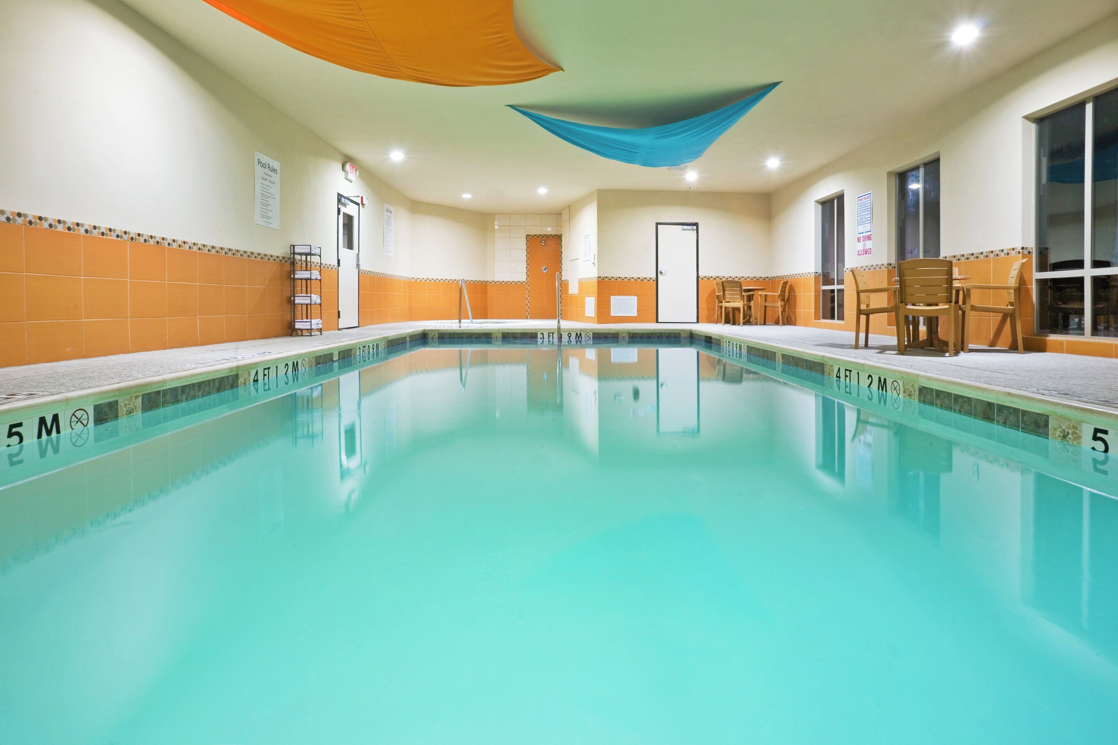 Piscina interior transparente com paredes azulejadas, uma porta e uma área de estar com cadeiras.