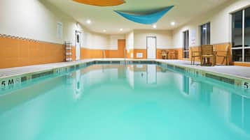 Piscina interior transparente com paredes azulejadas, uma porta e uma área de estar com cadeiras.