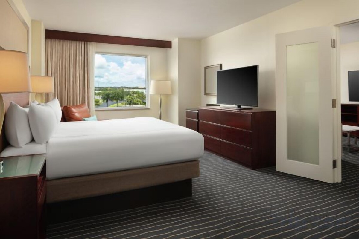 Quarto de hotel com cama, televisão, escrivaninha e janela com vista.