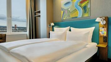 Quarto de hotel com uma cama grande, vista para uma ponte e um quadro abstrato colorido na parede.