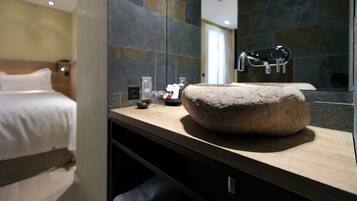Um banheiro moderno com uma pia grande de pedra, um espelho e uma cama ao fundo.