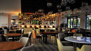 Um restaurante com mesas e cadeiras redondas, um espaço de bar com prateleiras cheias de garrafas e globos de vidro pendurados.