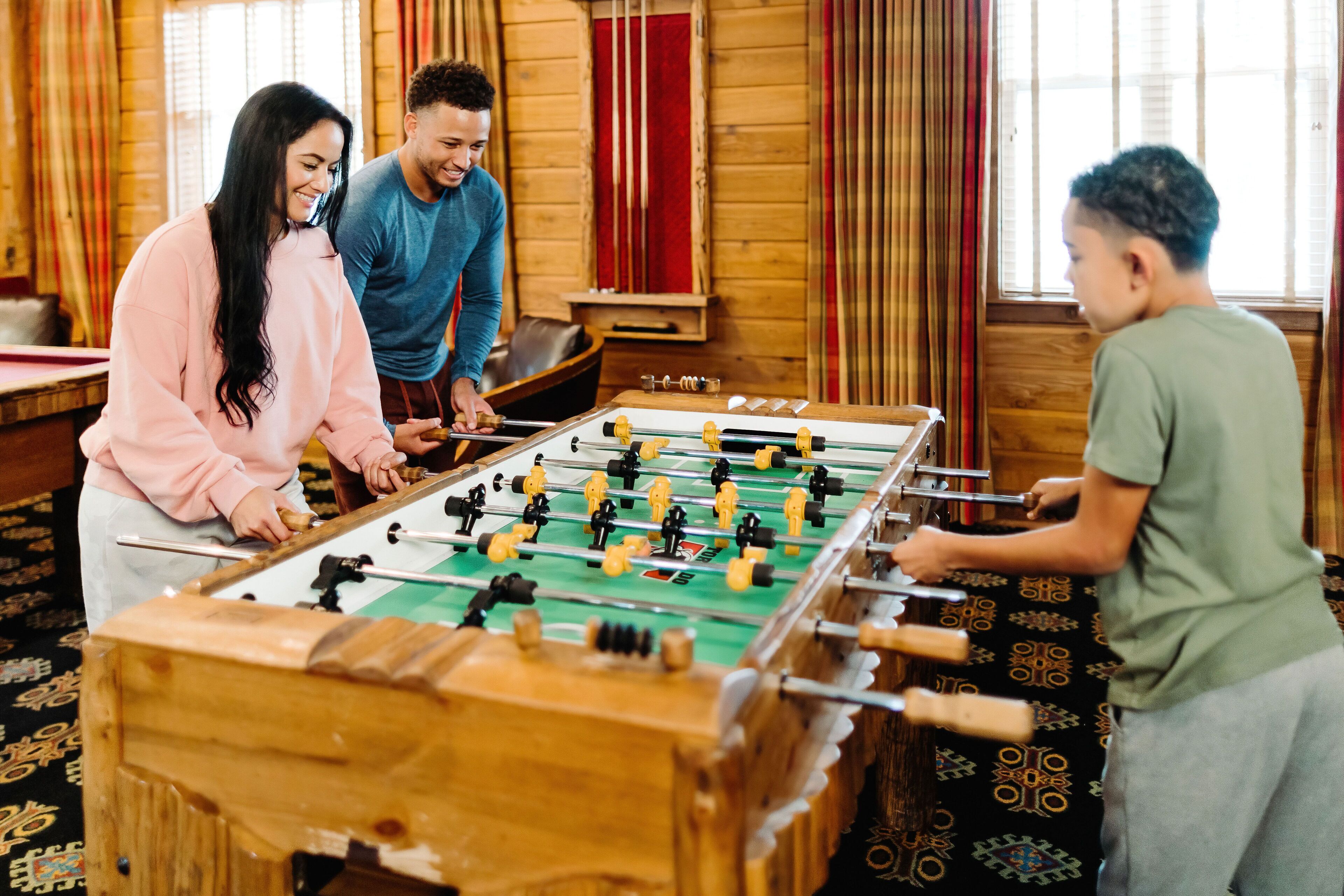 Uma mesa de futebol de madeira num espaço com paredes de madeira e um tapete estampado.