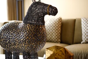 Escultura de um cavalo feita com materiais entrelaçados, colocada sobre uma superfície refletora.