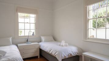 Quarto com duas camas, uma mesinha de cabeceira, cômoda e janela.